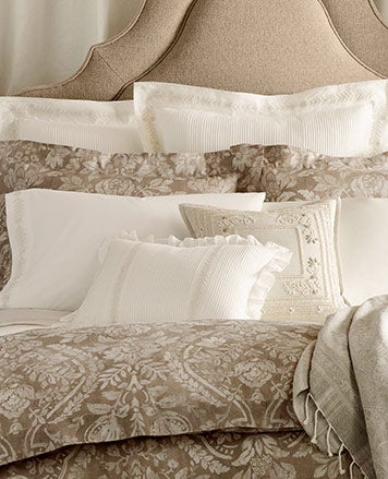 Bed appointed with neutral-hued sheeting with a 19th-century damask pattern
