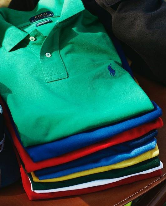 Boy in white Polo shirt carries stack of colorful Polo shirts.